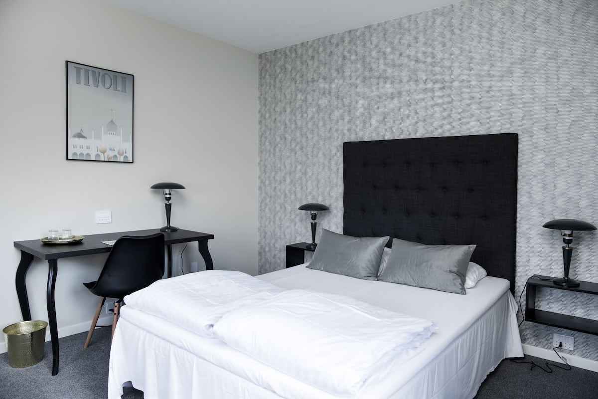 Quarto de hotel moderno com uma cama grande, uma escrivaninha e duas mesas de cabeceira.