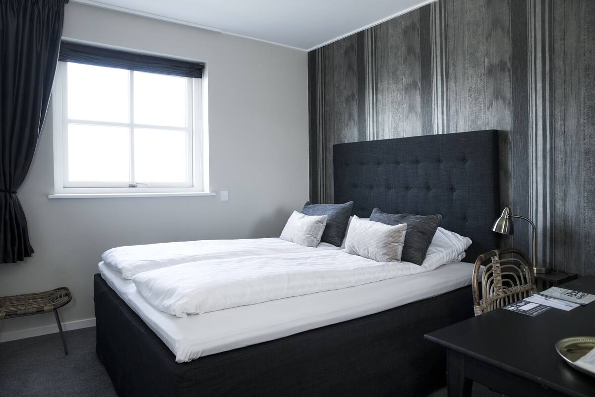Quarto moderno com uma cama grande, uma escrivaninha e uma janela com cortinas.
