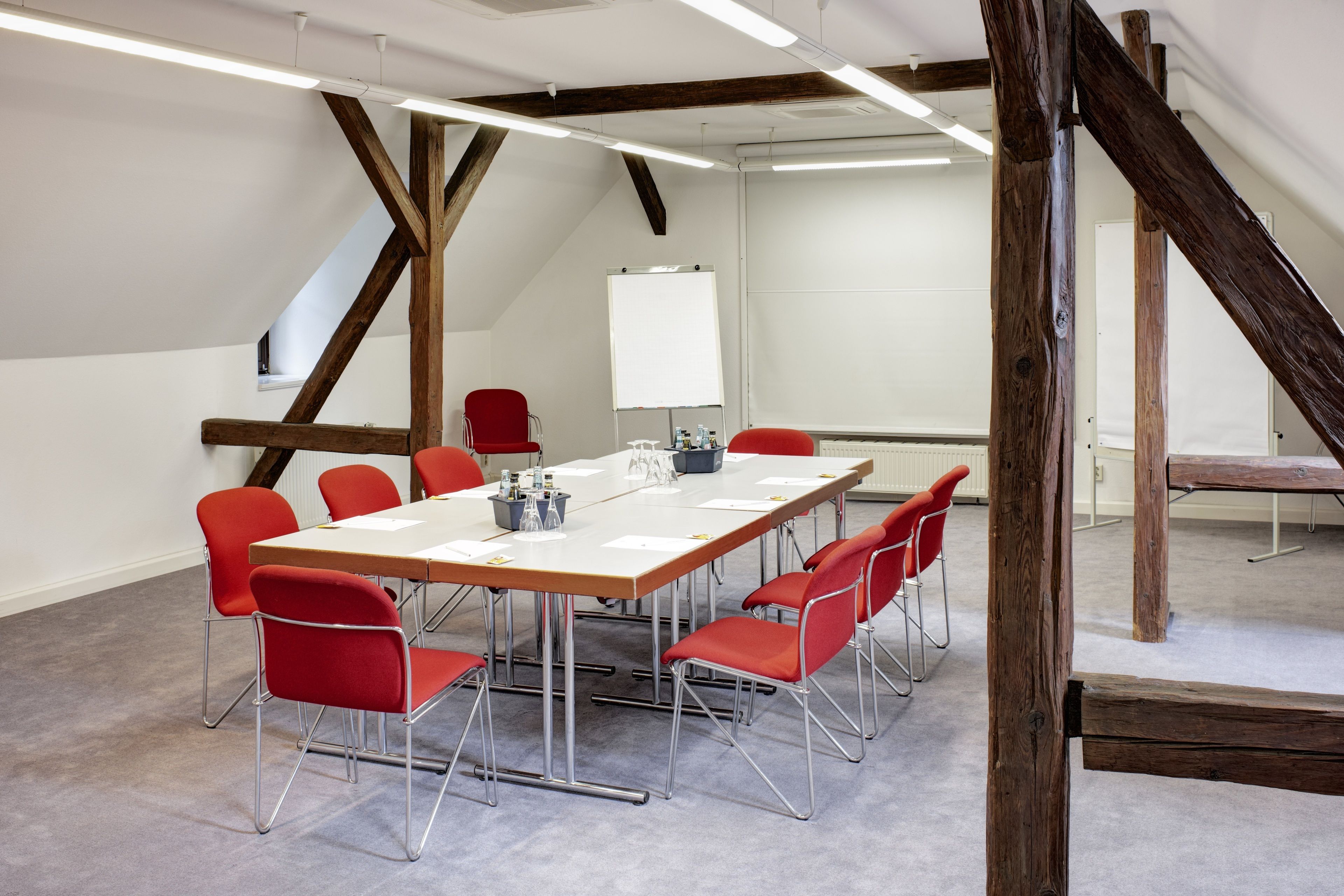 Uma sala de conferências com uma mesa comprida, cadeiras vermelhas e um quadro branco.