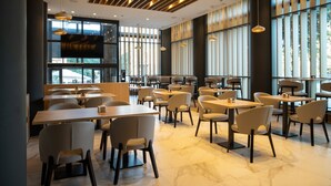 Um restaurante moderno com interior limpo e minimalista, apresentando uma mistura de mesas e cadeiras redondas e retangulares, janelas amplas e uma televisão de tela plana fixada na parede.