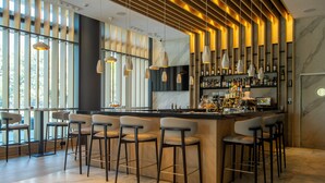 Uma área de bar moderna com uma ilha central, banquetas, luminárias pendentes e bancada de mármore.