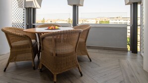Varanda com móveis de vime e uma mesa, com vista para a paisagem urbana.