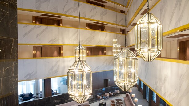 Um hall amplo com um balcão de recepção extenso, diversas áreas de estar e lustres geométricos pendentes.