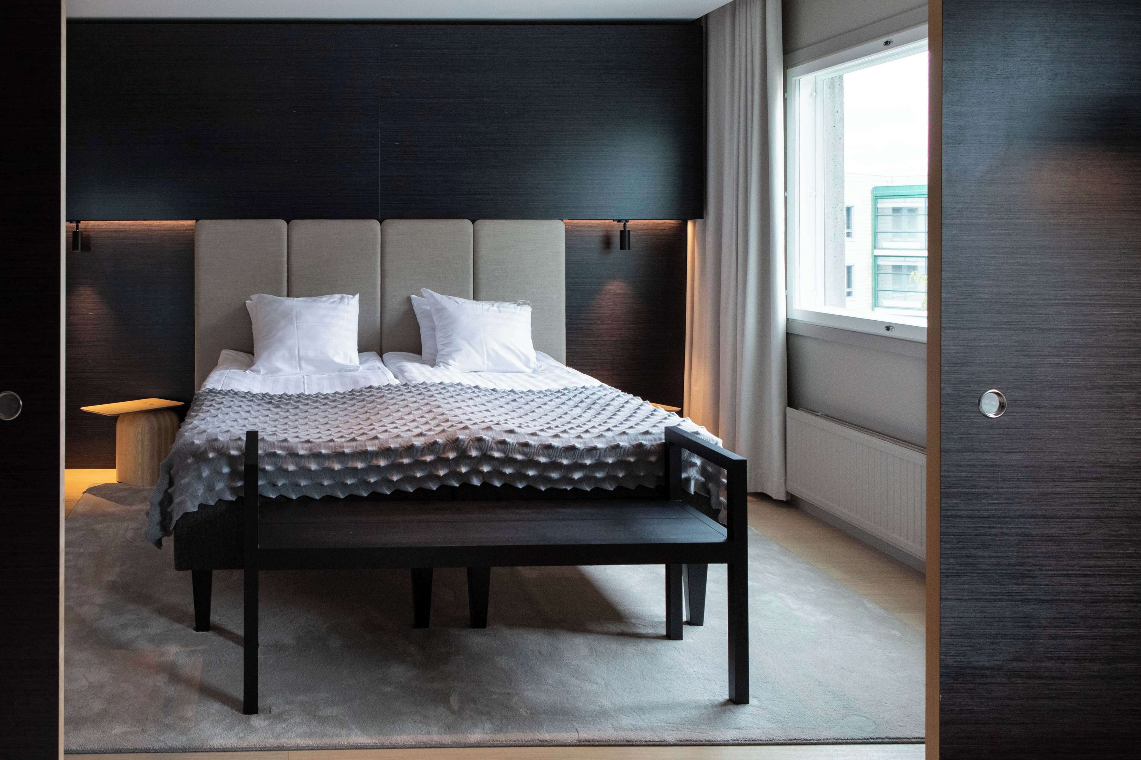 Um quarto moderno com cama, banco e mesa de cabeceira.