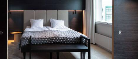 Um quarto moderno com cama, banco e mesa de cabeceira.
