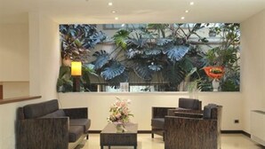 Um saguão com balcão de recepção, dois sofás, uma mesa de centro e uma janela ampla com vista para plantas tropicais.