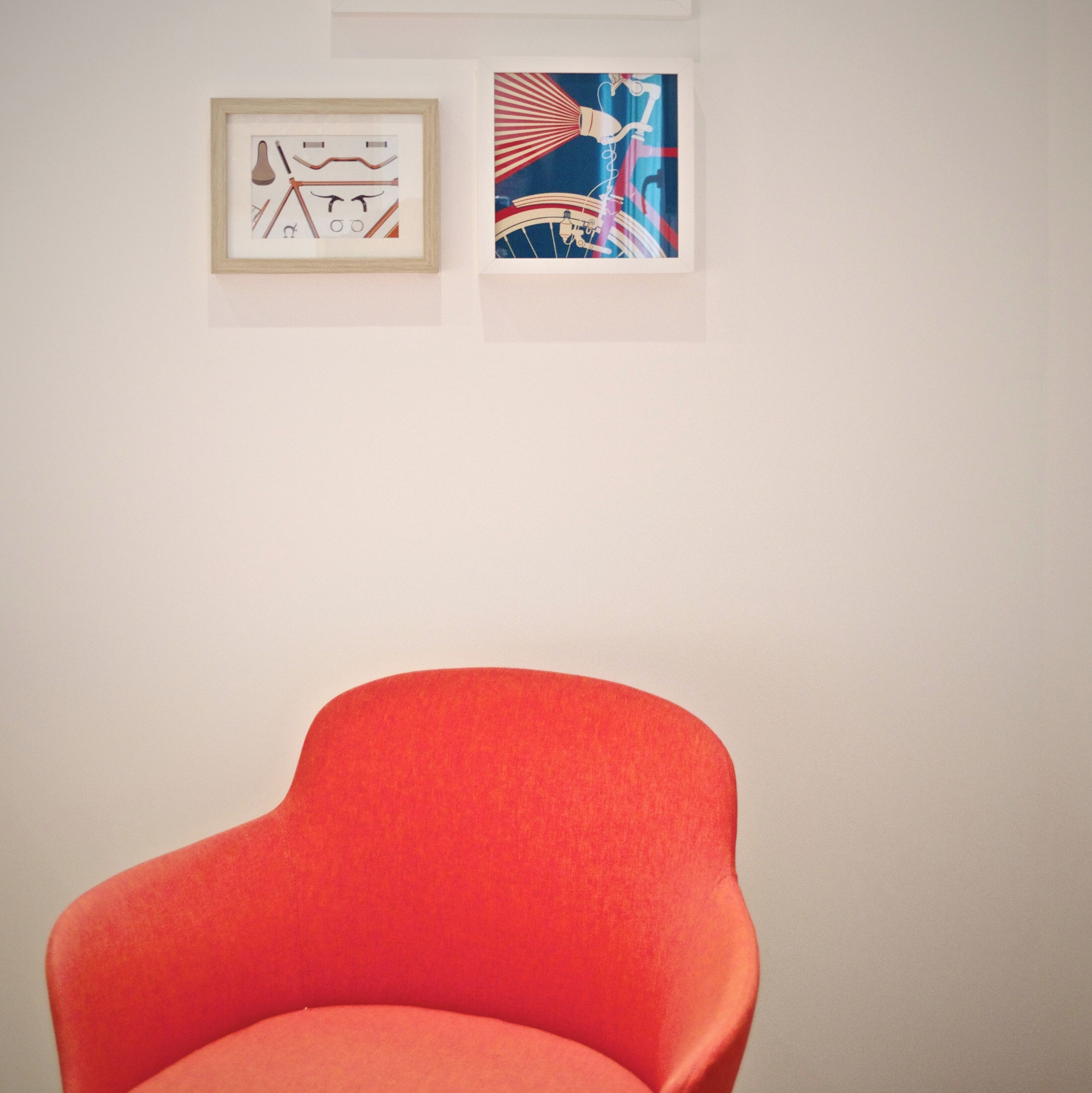 Um quarto com uma cadeira vermelha e duas obras de arte emolduradas na parede.