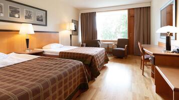 Quarto de hotel com duas camas, uma escrivaninha, uma cadeira e uma mesinha.