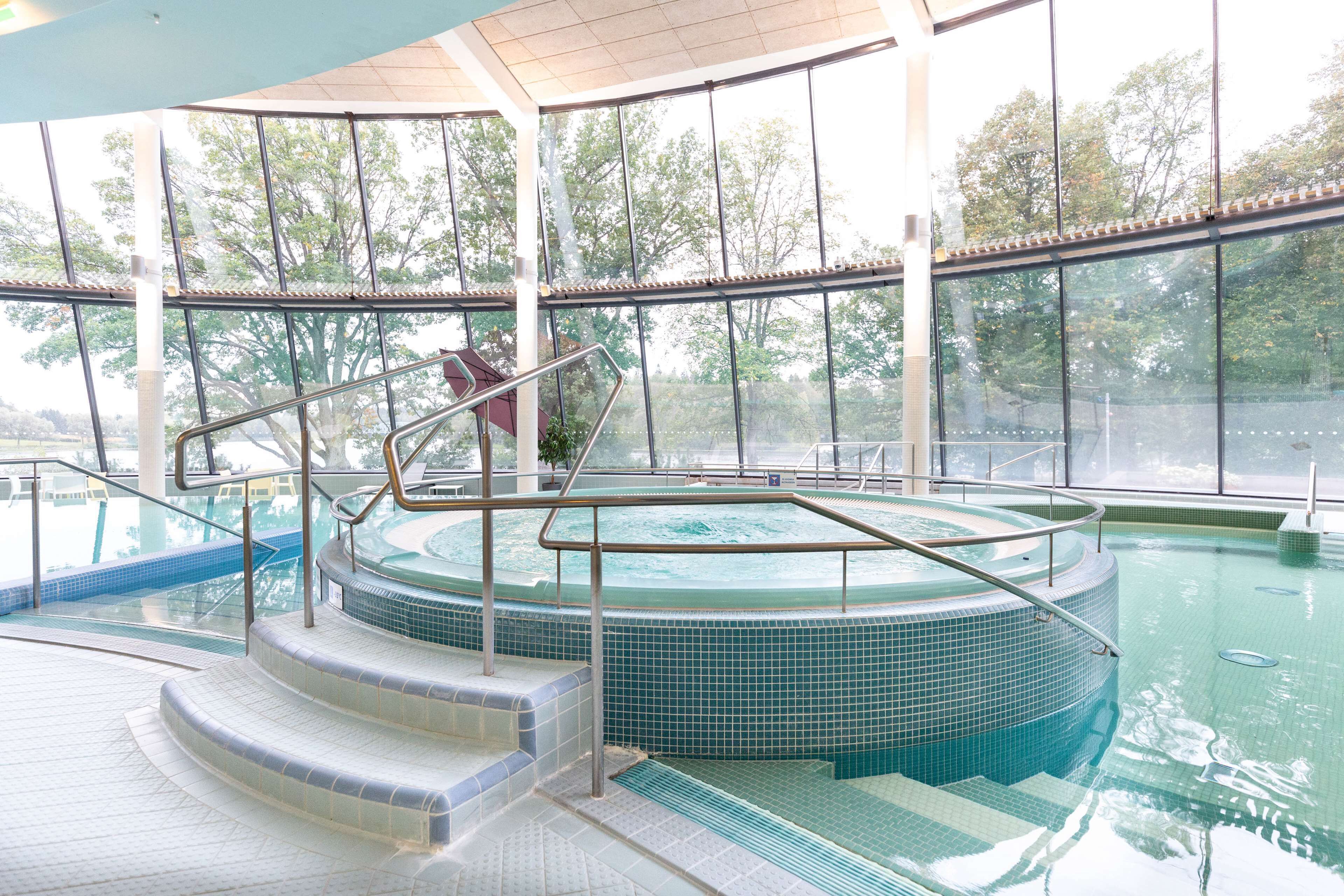 Piscina interior com teto de vidro, banheira de hidromassagem e escadaria que dá para a piscina.