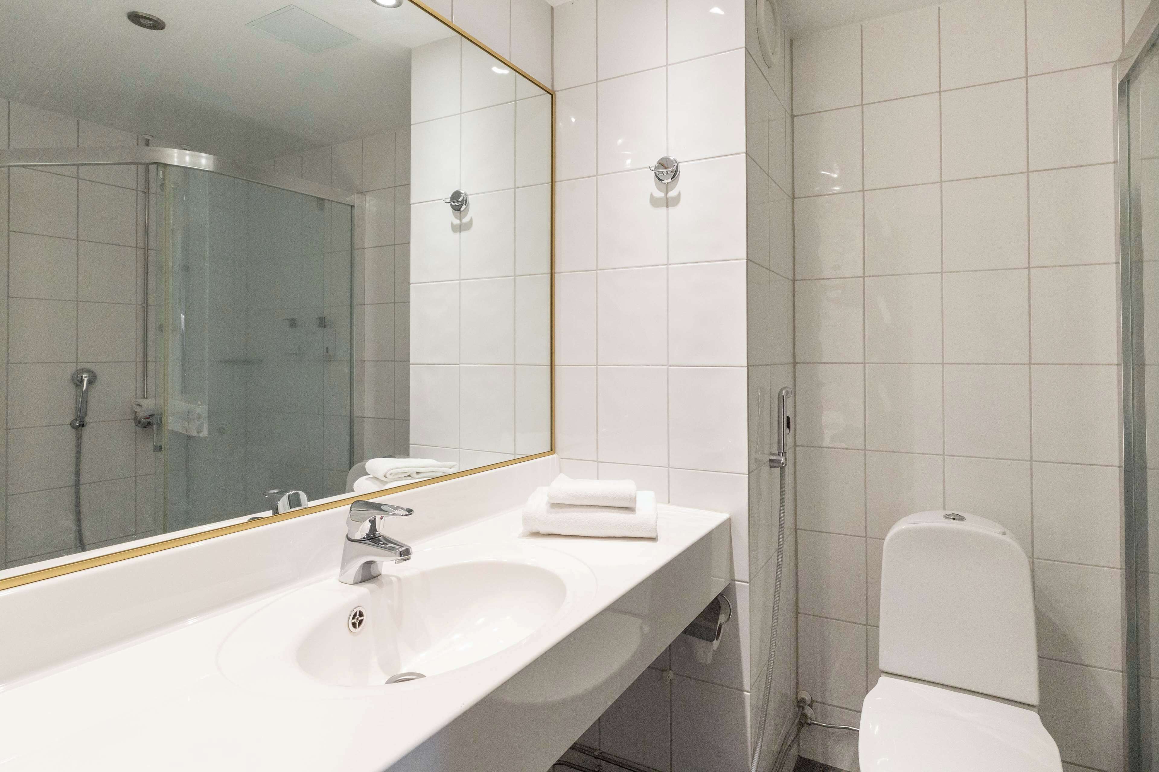 Uma casa de banho moderna com um espelho grande, duas lavatórios, chuveiro e sanita.