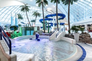 Parque aquático interno com banheira de hidromassagem, toboáguas e palmeiras.