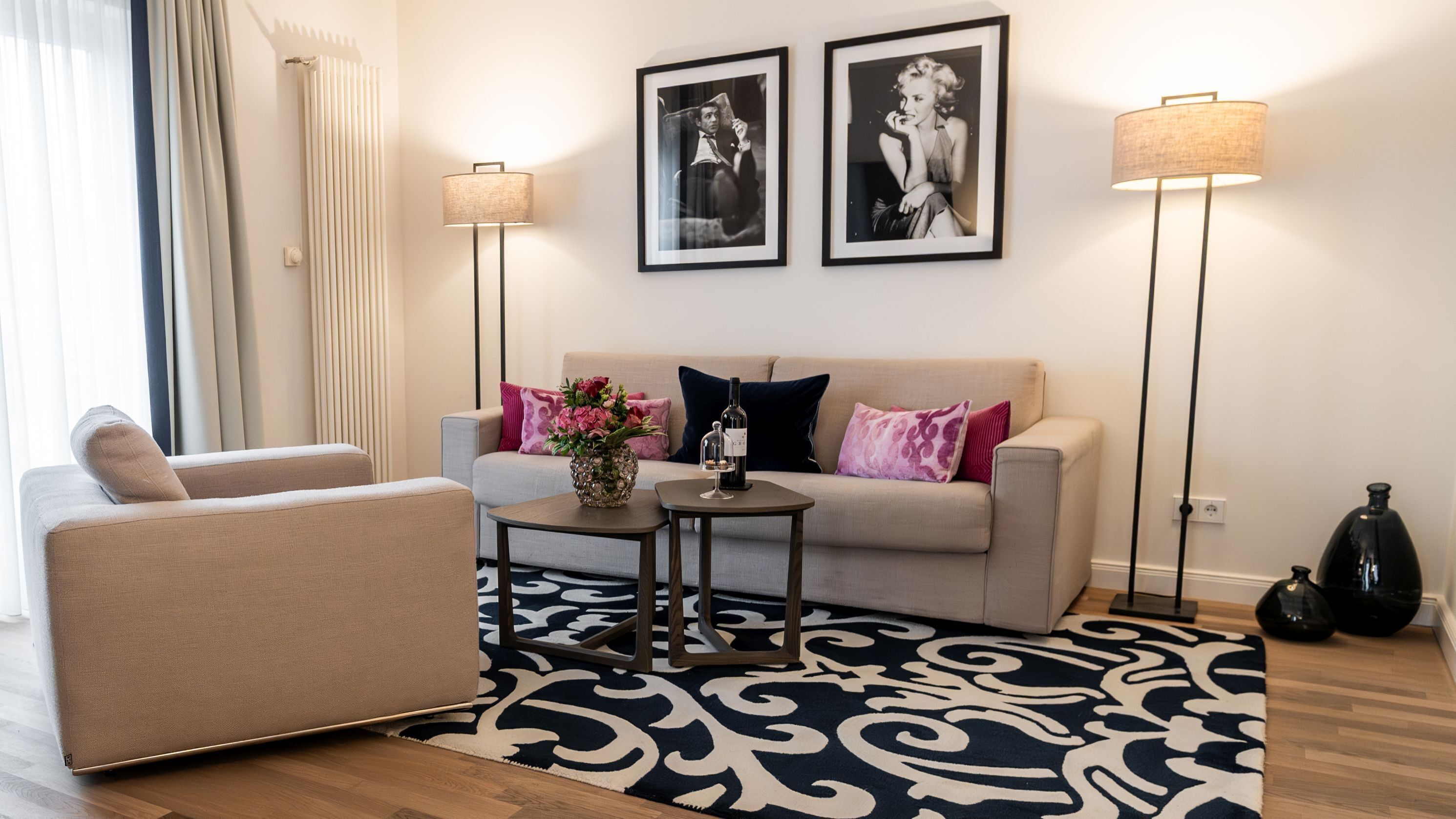 Uma sala de estar com sofá, poltrona, mesa de centro e duas luminárias de chão.