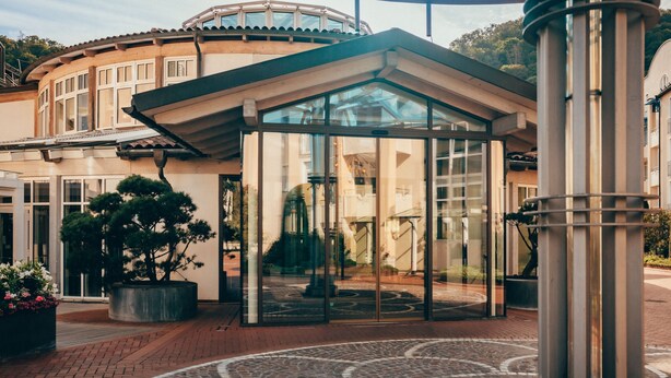 Um edifício com entrada de vidro, caminho de tijolos e um grande vaso com uma árvore.
