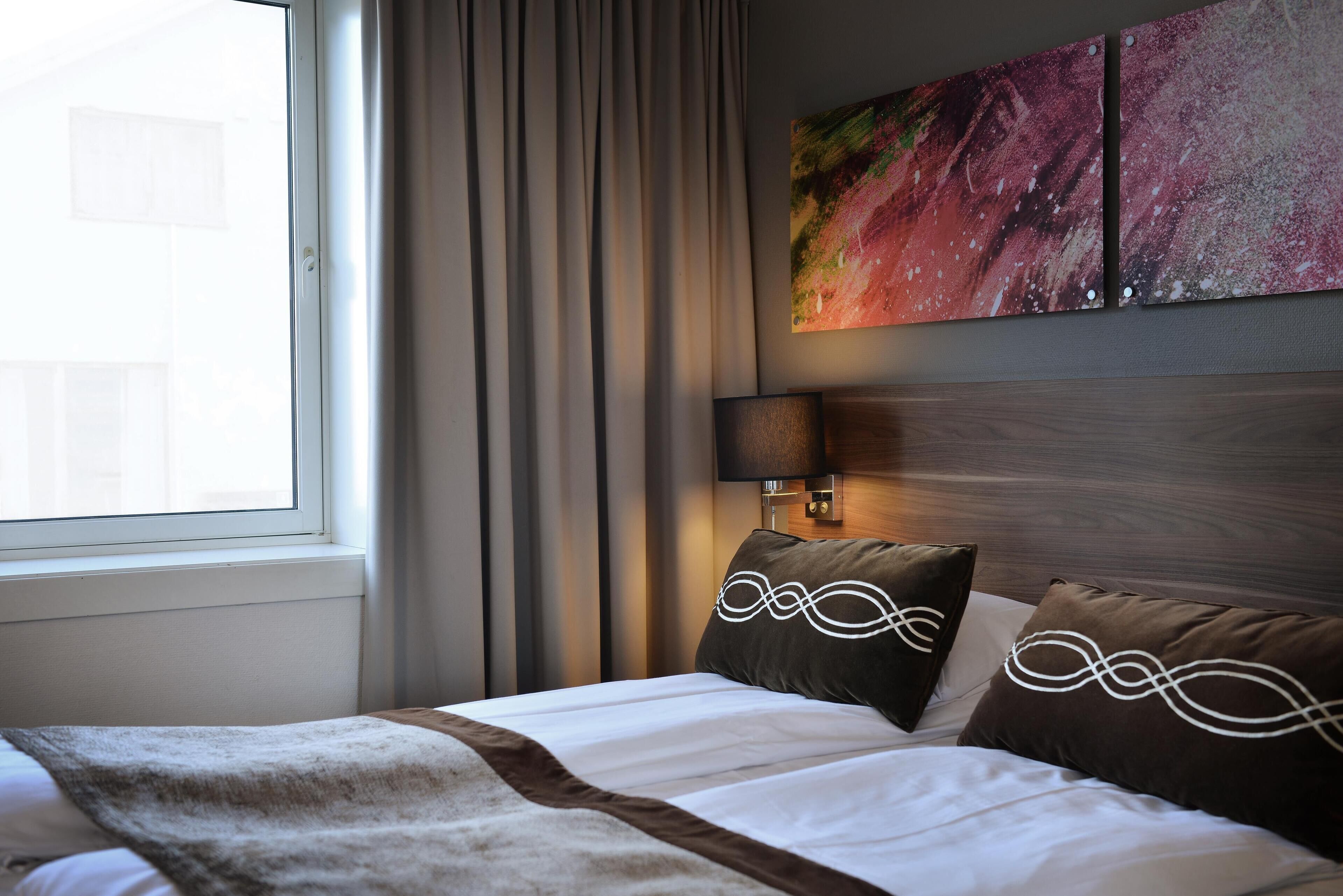 Quarto de hotel com cama, cortinas, luminária na parede e um quadro.