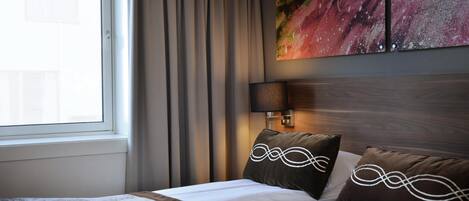 Quarto de hotel com cama, cortinas, luminária na parede e um quadro.