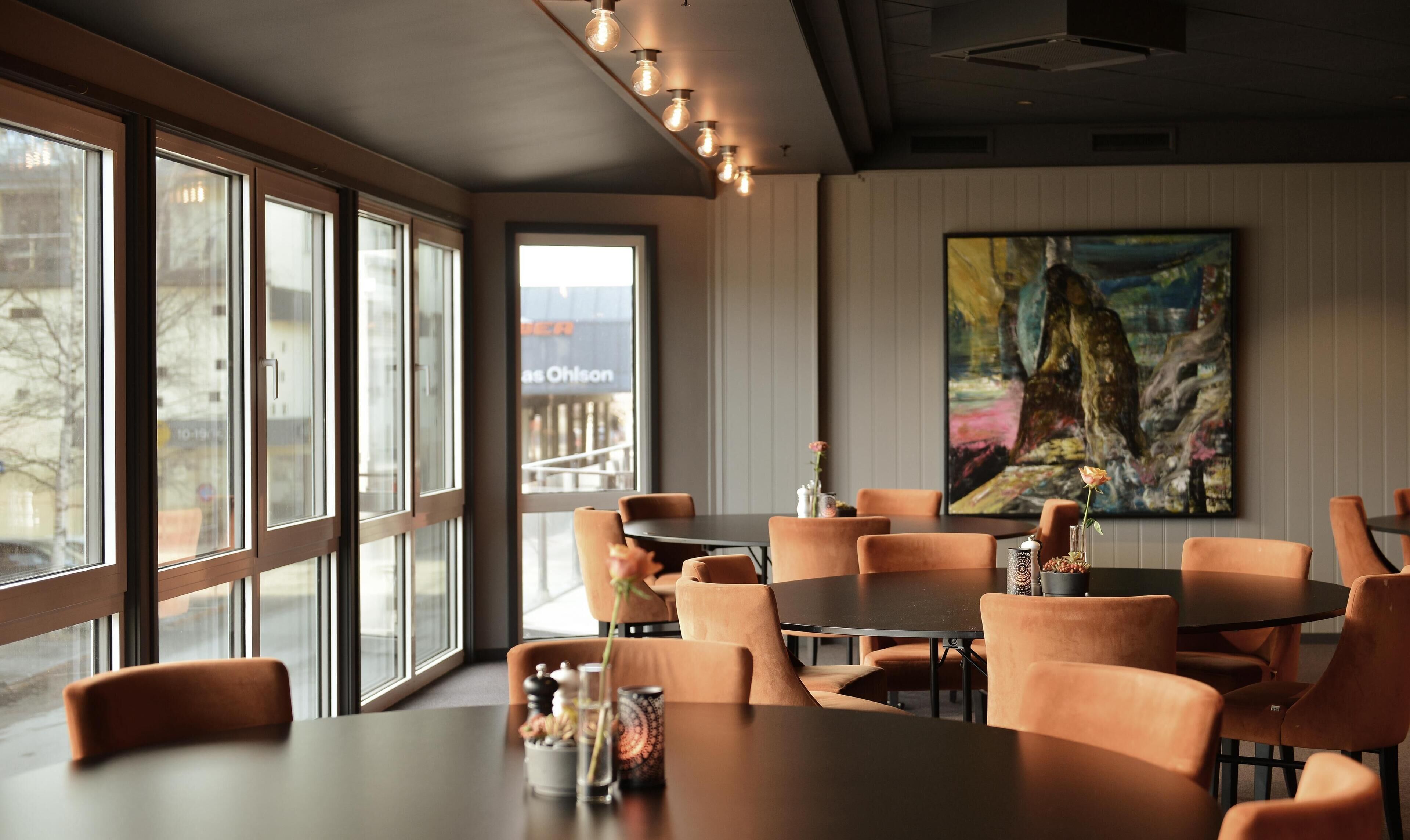 Uma sala de jantar moderna com grandes janelas, uma pintura grande na parede e diversos tipos de assentos.