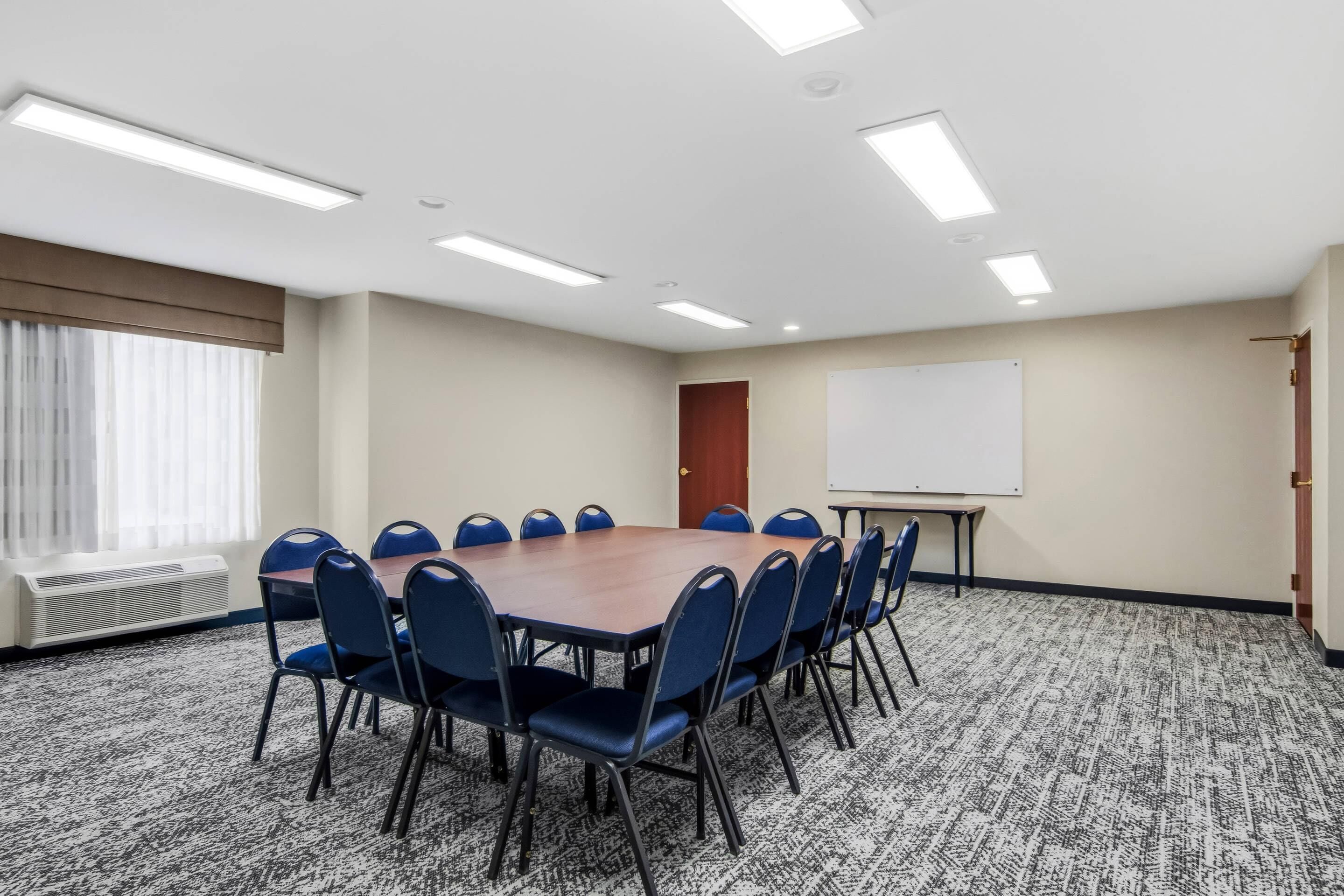 Uma sala de conferência com uma grande mesa, cadeiras azuis, um quadro branco e piso carpeteado.