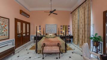 Quarto com cama, escrivaninha, cadeira, ventilador de teto e uma janela grande com cortinas.