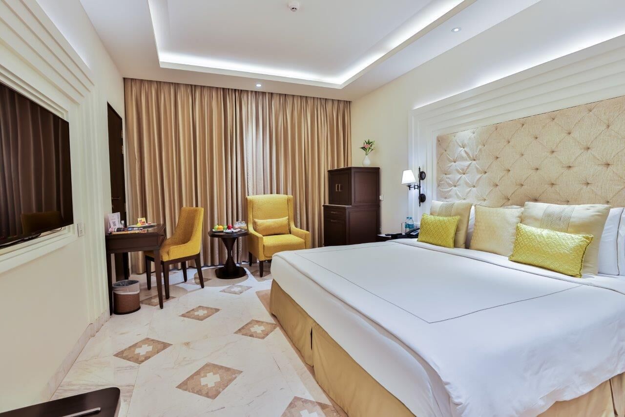 Quarto de hotel com uma cama grande, uma escrivaninha com cadeira, um guarda-roupa e uma televisão.