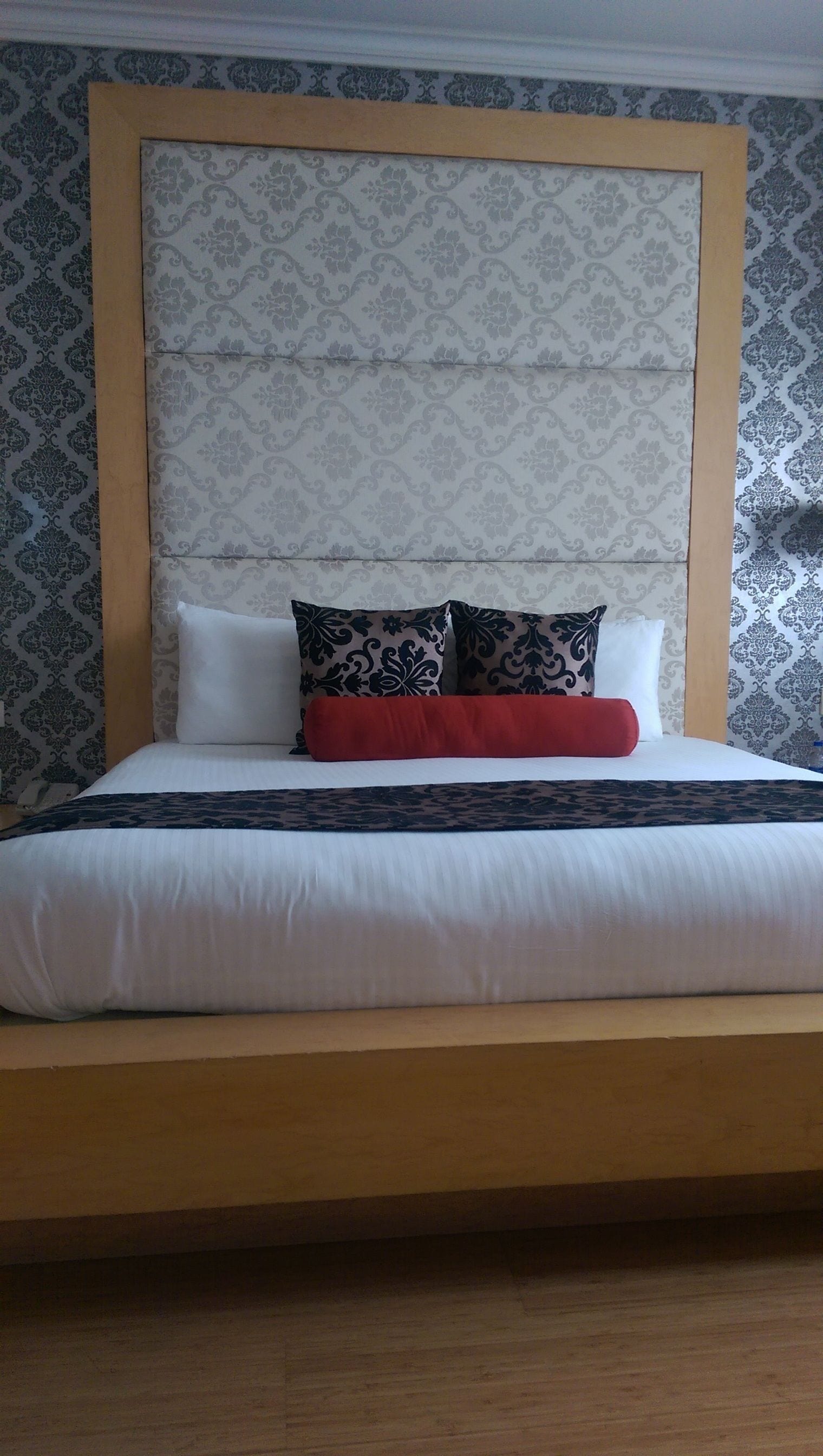 Uma cama bem arrumada com cabeceira de madeira, roupa de cama branca e almofadas estampadas.