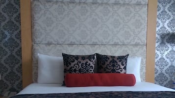 Uma cama bem arrumada com cabeceira de madeira, roupa de cama branca e almofadas estampadas.