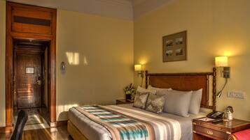 Quarto de hotel com uma cama grande, cabeceira de madeira, duas mesas de cabeceira com luminárias, um criado-mudo e uma cadeira vermelha.