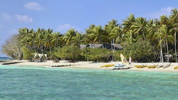 Uma praia com águas turquesa cristalinas, palmeiras e vários barcos pequenos.