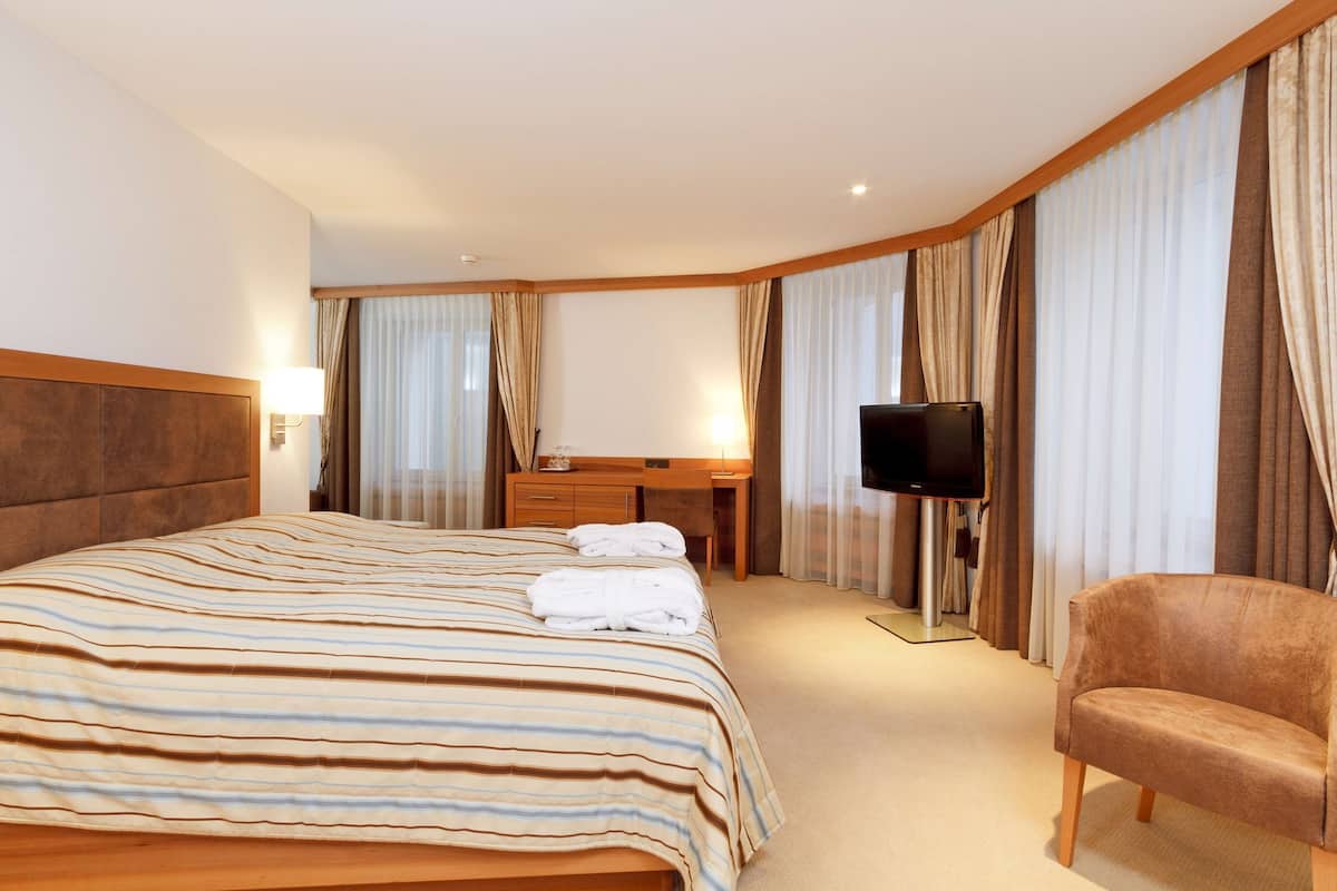 Quarto de hotel com uma cama grande, uma escrivaninha, uma cadeira e uma televisão.