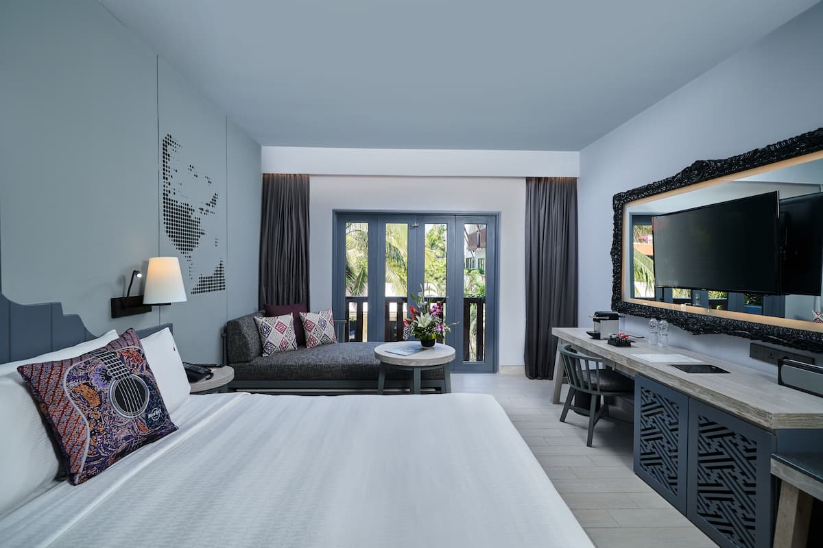 Quarto de hotel moderno com uma cama grande, um sofá, um espaço de refeições e uma televisão.
