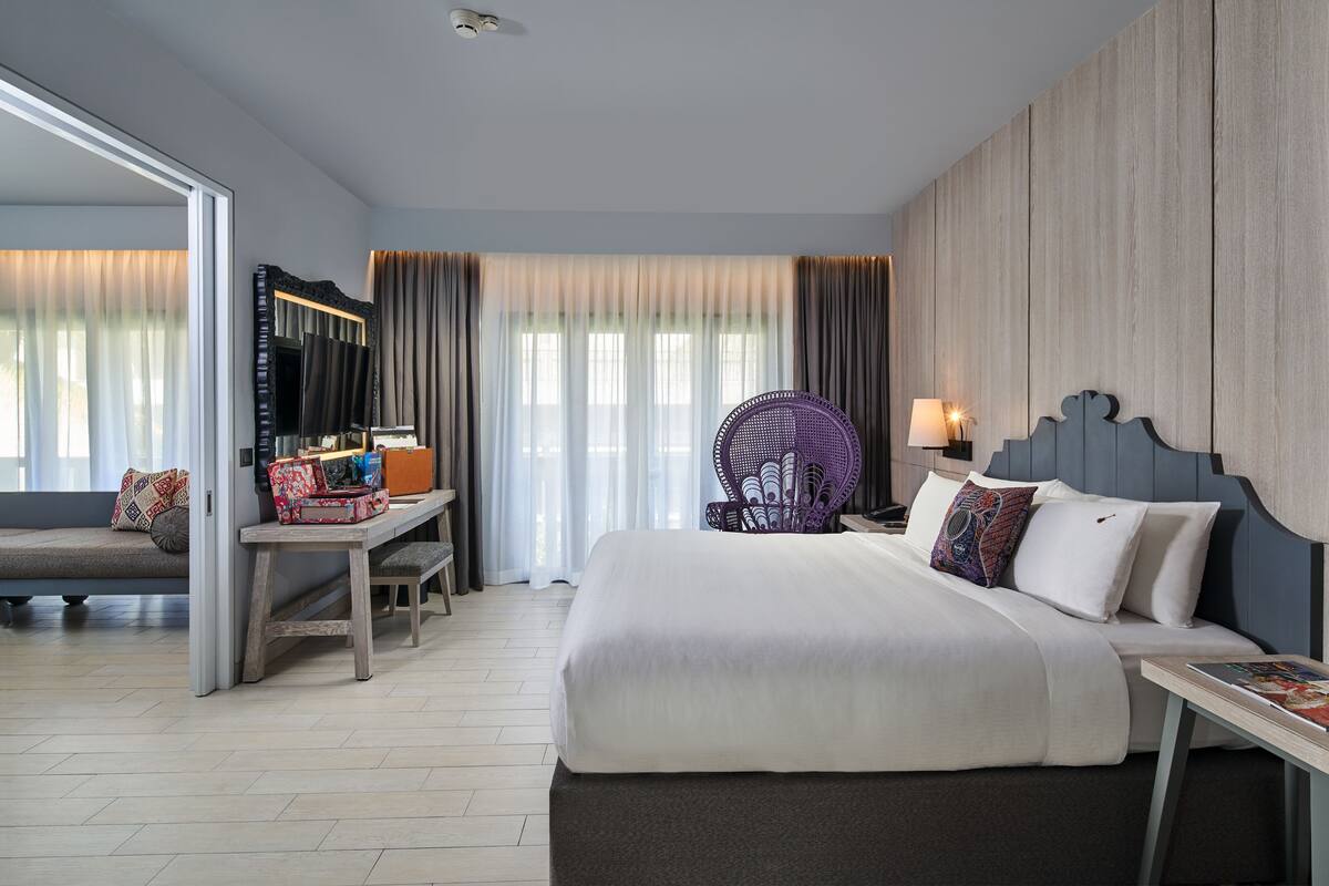 Quarto de hotel com uma cama grande, uma escrivaninha com cadeira, televisão e janela com cortinas.