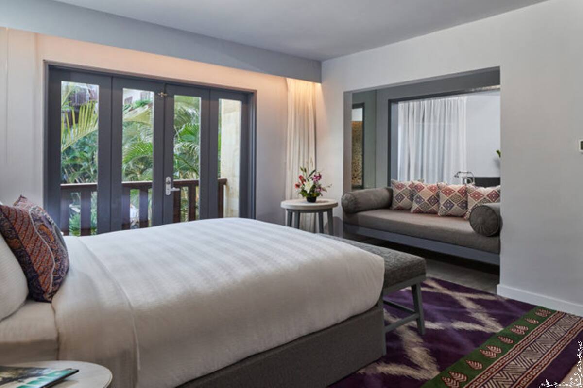 Quarto de hotel moderno com uma cama grande, um sofá, uma mesinha com um vaso e uma varanda com vista para o verde.