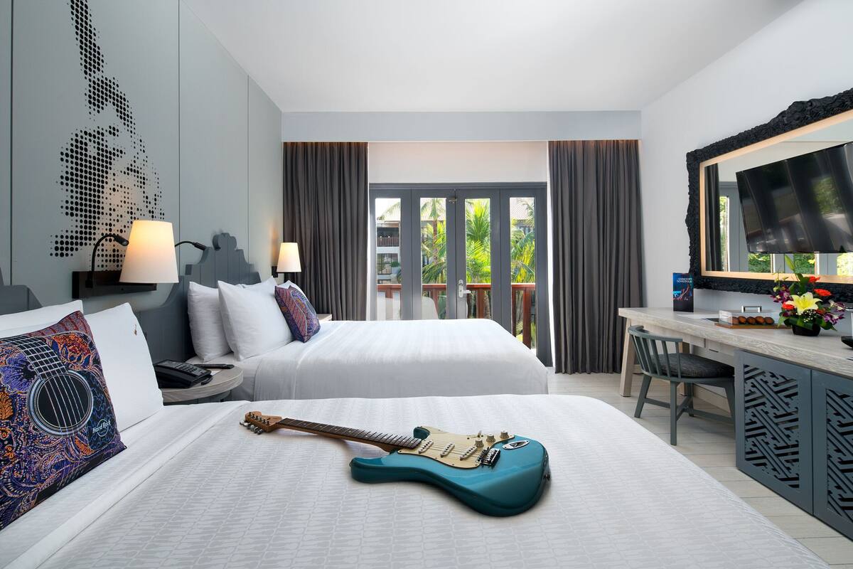 Quarto de hotel com uma cama, uma mesa, uma guitarra e uma televisão.