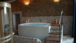 Uma área de spa com hidromassagem, degraus de pedra e sauna envidraçada.