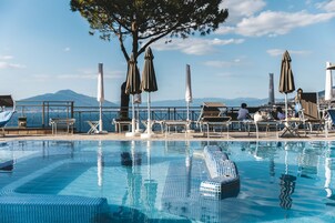 Uma área de piscina com espreguiçadeiras e guarda-sóis, vista desobstruída das montanhas e um corrimão com vista para a água.