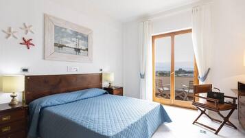Quarto de hotel com cama, escrivaninha, cadeira e varanda com vista.