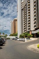 Um hotel com vários andares, uma entrada em curva e carros estacionados.