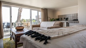 Quarto com cama grande, mesa de cabeceira de madeira, vista para a varanda e backsplash de azulejos.