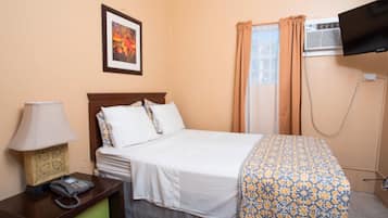 Quarto de hotel com cama, mesa de cabeceira com abajur e telefone, quadro na parede e ar condicionado.
