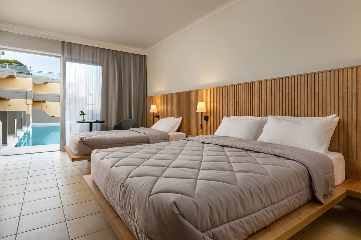 Quarto de hotel com uma cama grande, uma cama menor, uma escrivaninha e vista para uma piscina.