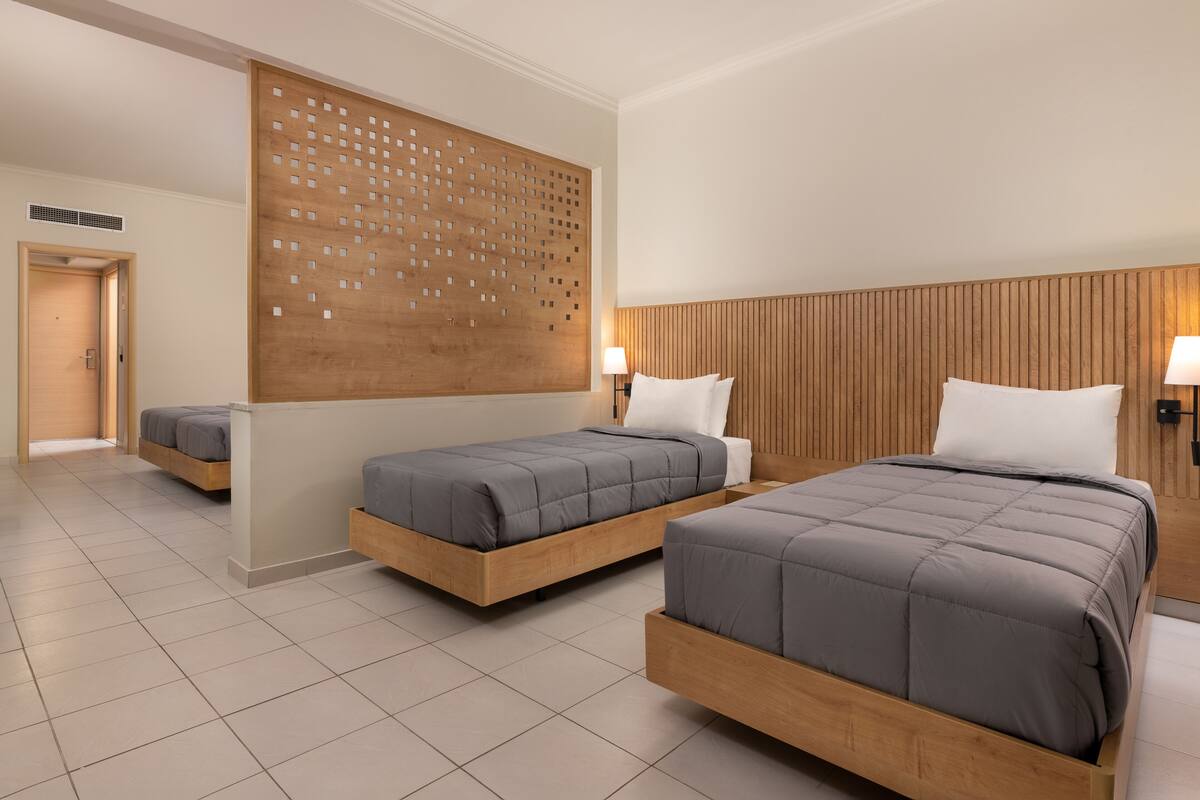 Quarto de hotel com duas camas, cabeceira de madeira, painel decorativo na parede e piso ladrilhado.