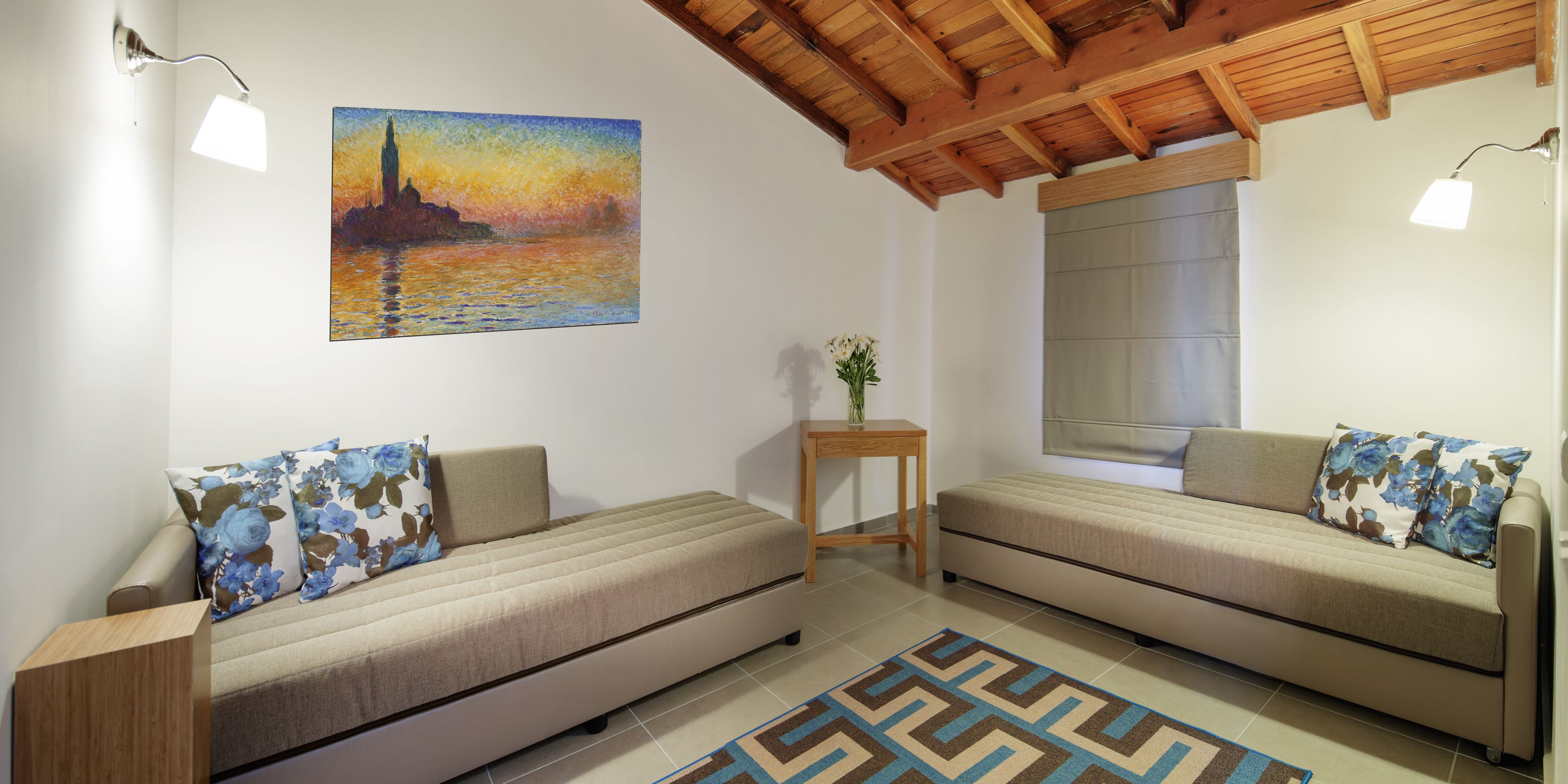 Quarto com dois sofás, uma pintura de paisagem urbana, uma pequena mesa de madeira com um vaso e uma janela com cortinas.