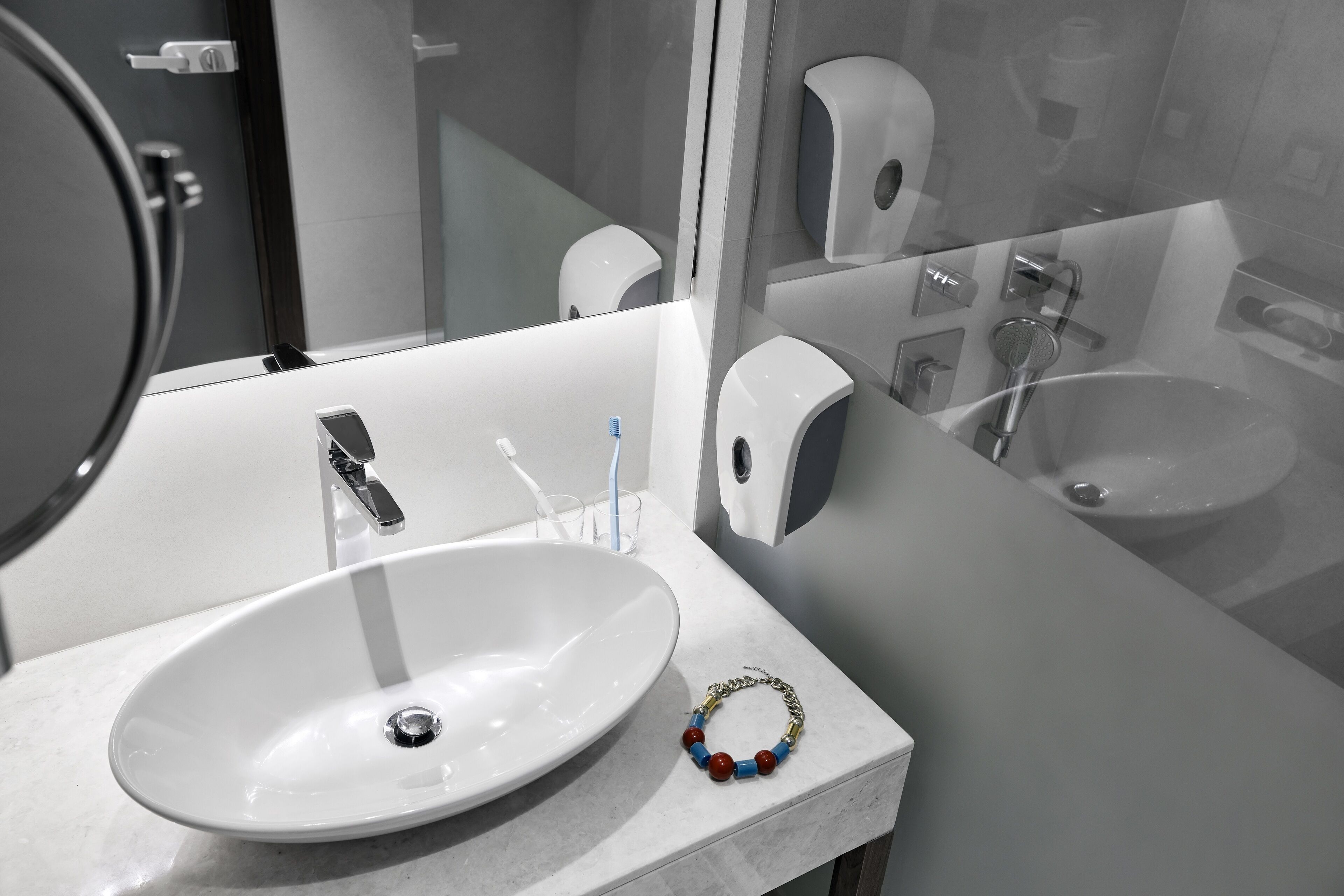 Casa de banho com lavatório branco, espelho, chuveiro manual e dispensador de sabonete.