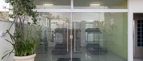 Entrada de um edifício moderno com porta de vidro, uma planta em vaso e um portão de metal.