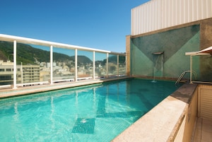 Piscina no terraço com vista ampla da cidade e montanhas ao fundo.