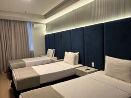Quarto de hotel com duas camas de solteiro, uma mesa de cabeceira com telefone e ar-condicionado fixado na parede.