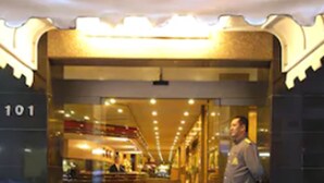 Um homem em frente à entrada de um edifício, com o número '101' visível na parede.