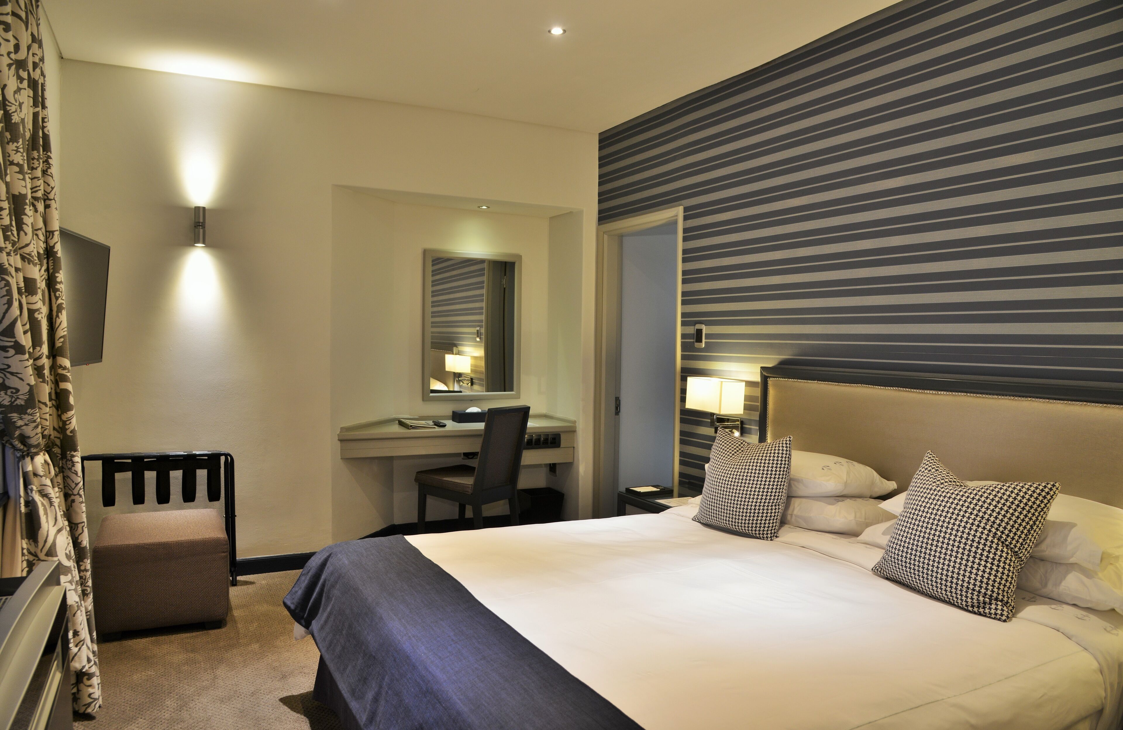 Quarto de hotel com cama, secretária, cadeira, televisão e uma janela grande.