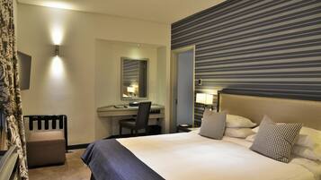 Quarto de hotel com cama, secretária, cadeira, televisão e uma janela grande.
