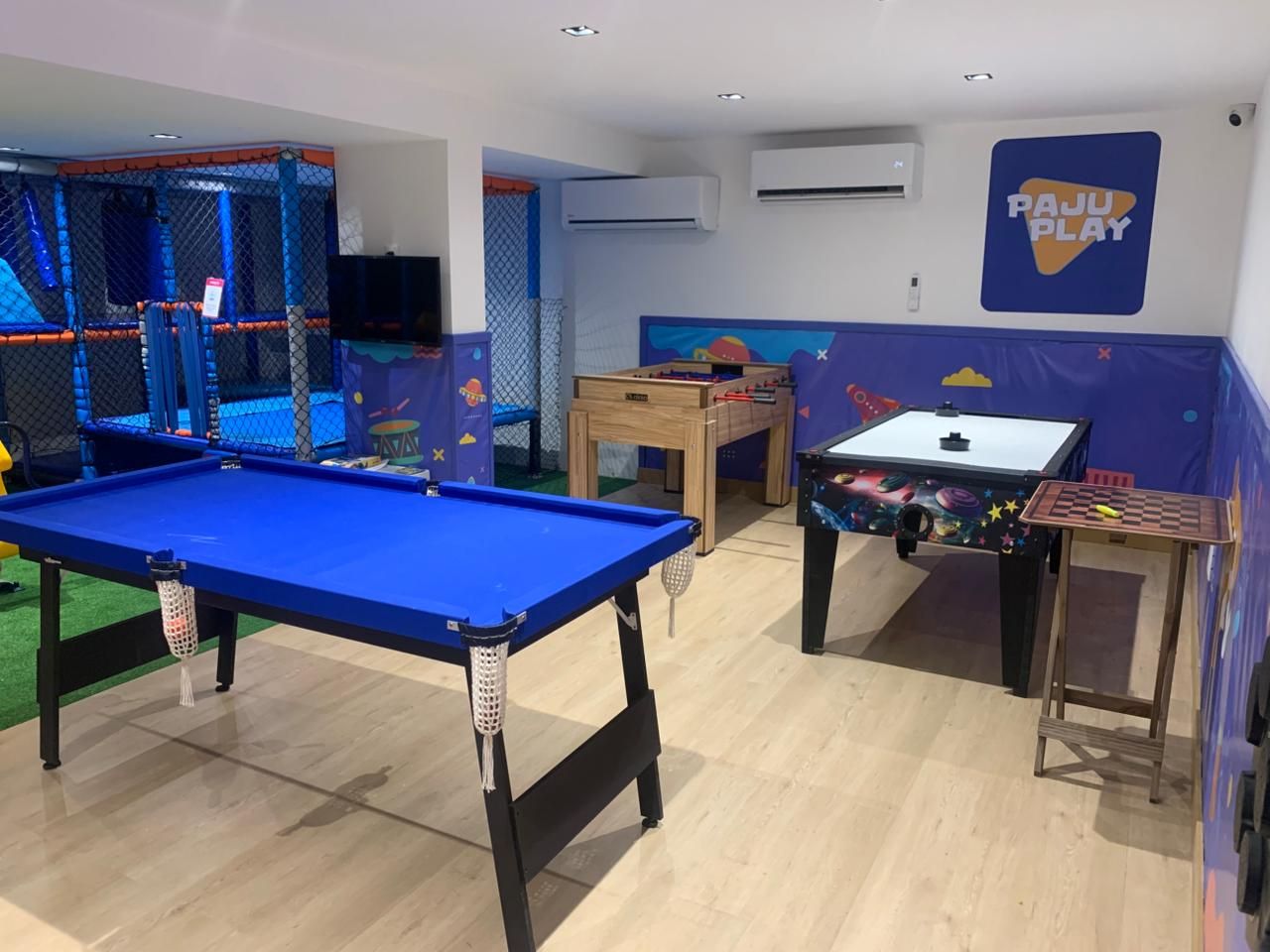 Sala de lazer com mesa de bilhar azul, mesa de pebolim e área de recreação com rede de escalada.
