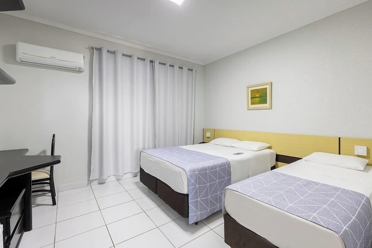 Quarto de hotel com duas camas, uma escrivaninha e janela com cortinas.